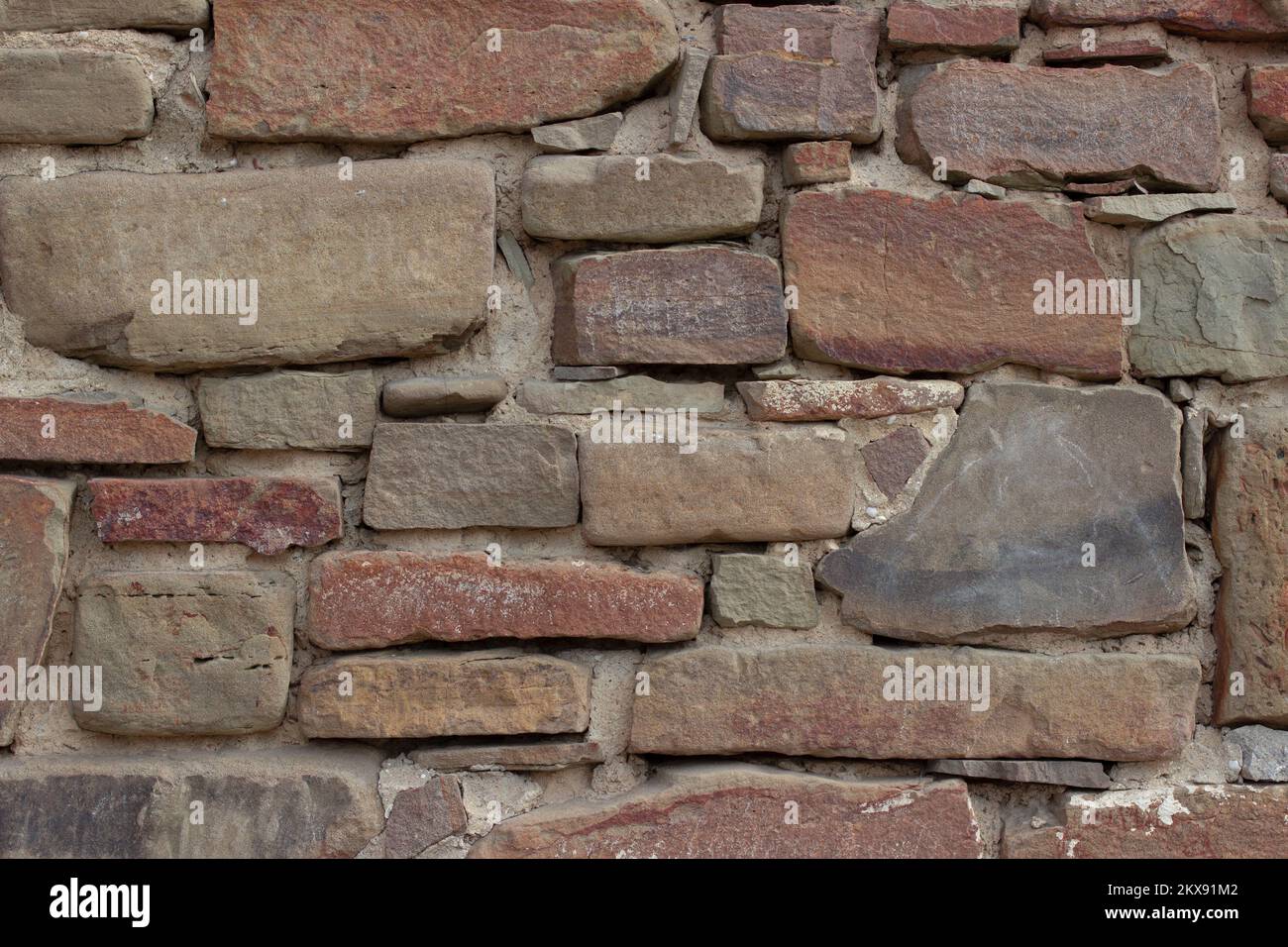 Old stone wall made of various square natural stones in beige, ocher ...