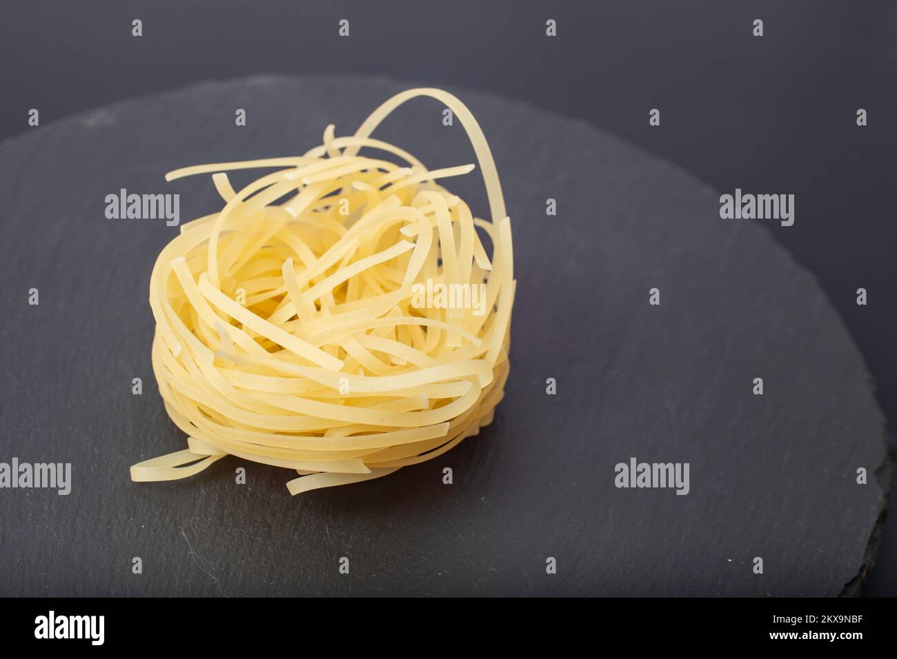 Thin pasta nest on a black stone tile, soft focus close up Stock Photo ...