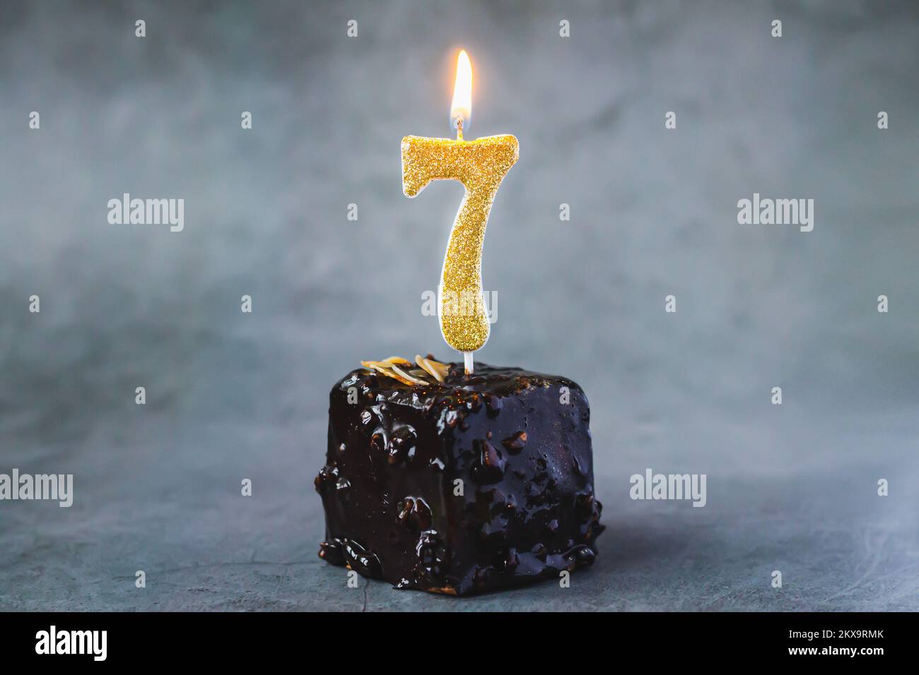 Birthday chocolate cake with number seven burning candle on dark ...