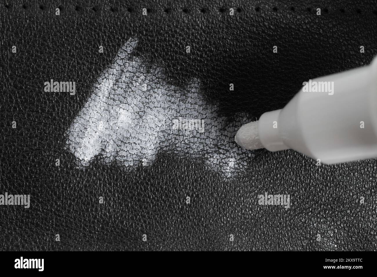 Scribbling with a white paint pen on black leather texture, soft focus ...