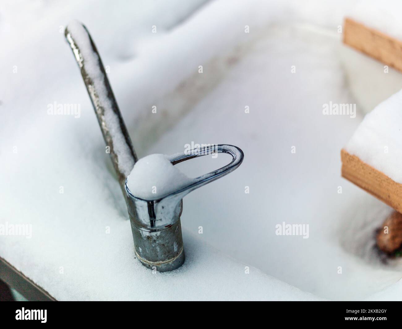 a frozen water tap and sink covered with ice and snow, outdoor closeup ...