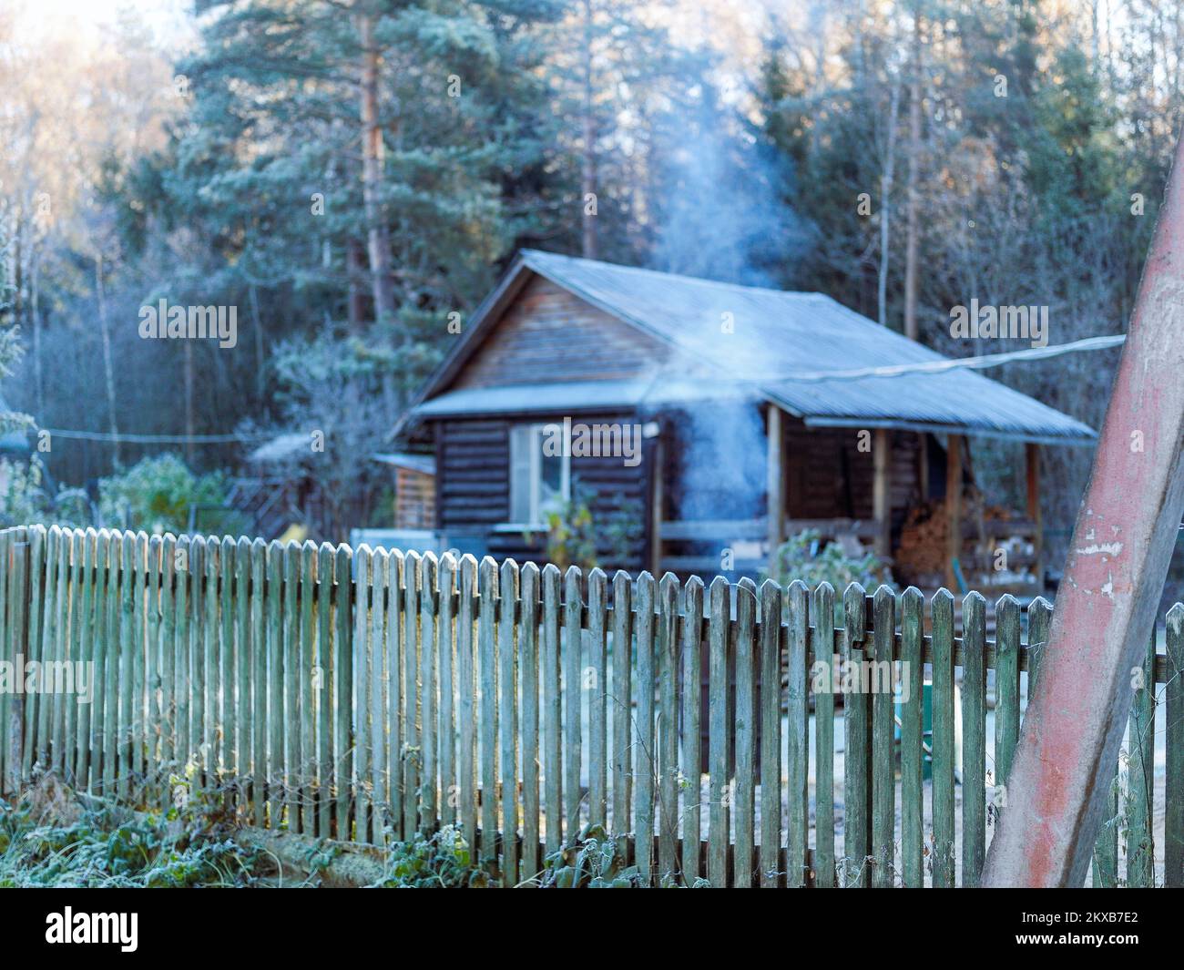 winter landscape with a wooden house and bonfire smoke in the yard ...