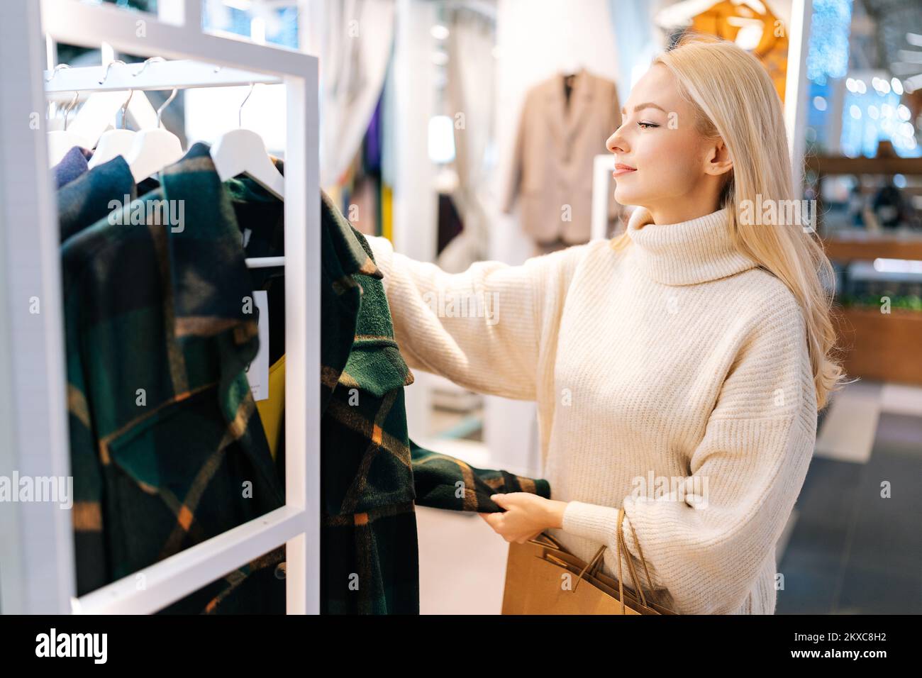 Side view of pretty young woman choosing coat in clothing store ...