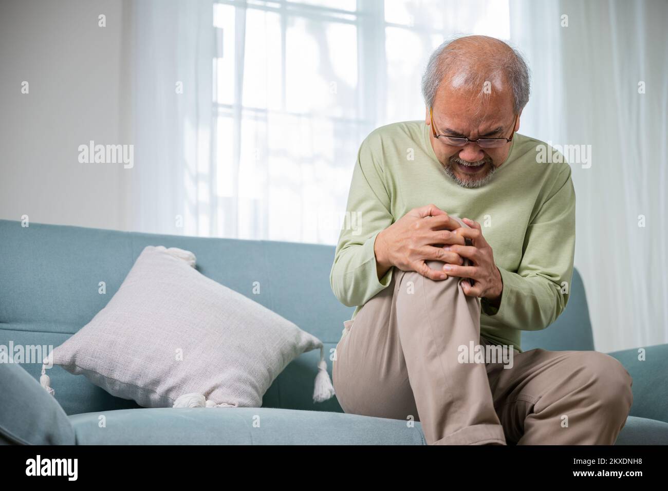 Asian senior man retirement knee joint pain on sofa Stock Photo - Alamy