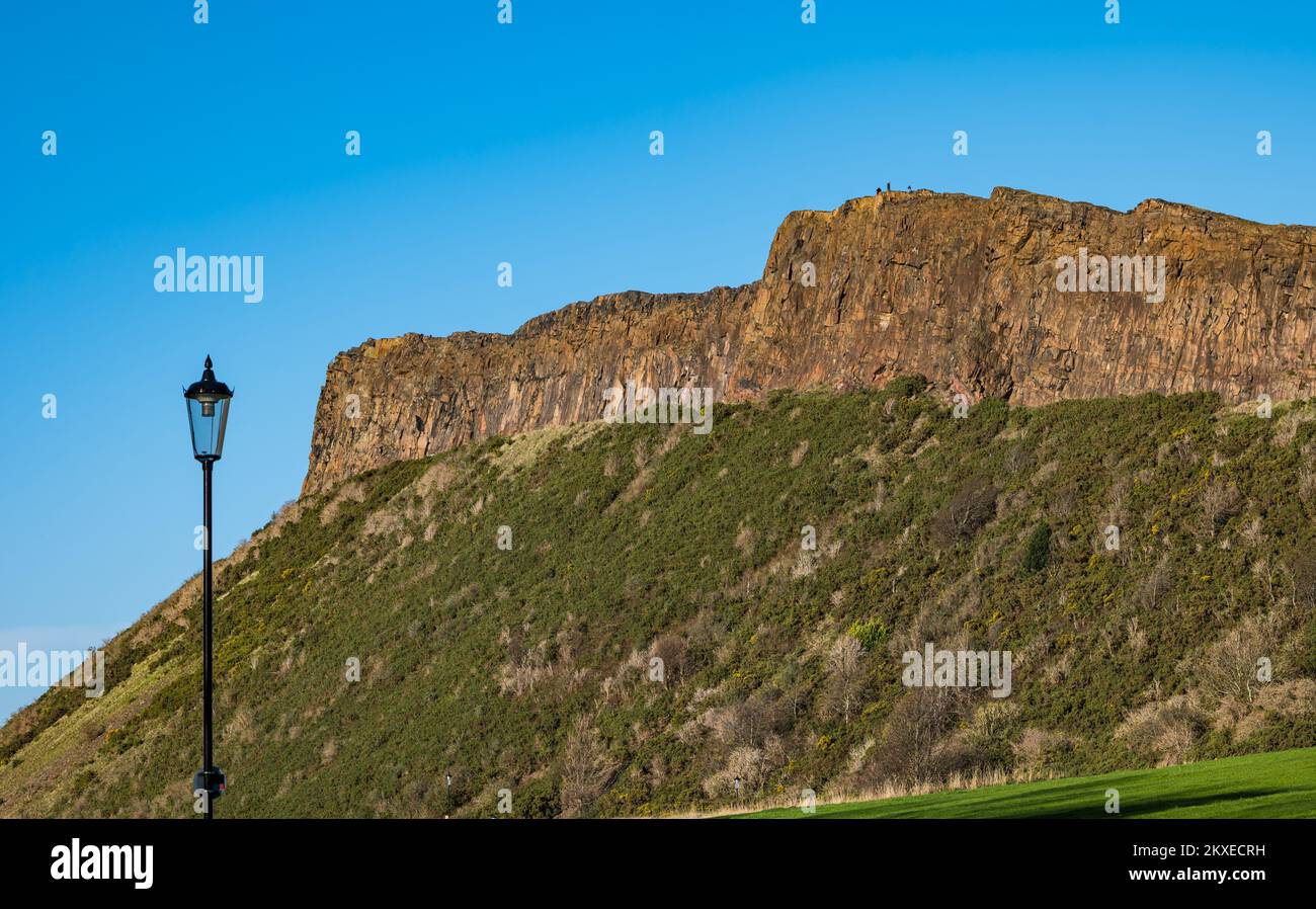View of people clifftop ledge on Salisbury Crags, a rocky cliff in ...