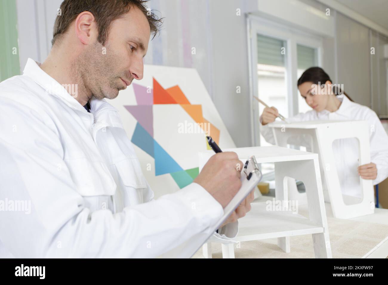 foreman writing on clipboard while female apprentice paints Stock Photo ...