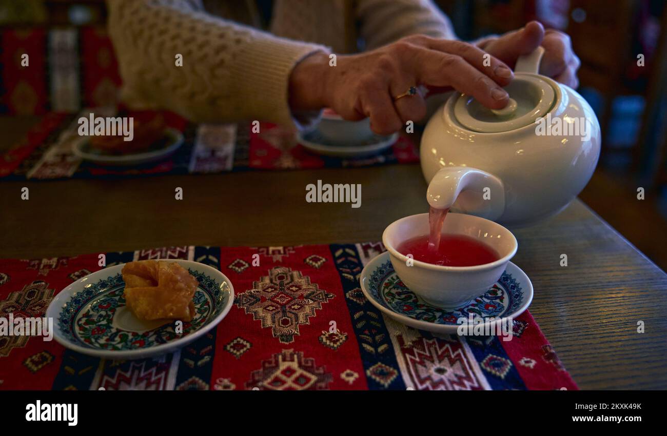 Anonymous woman pours tea from a white ceramic teapot into a cup and ...