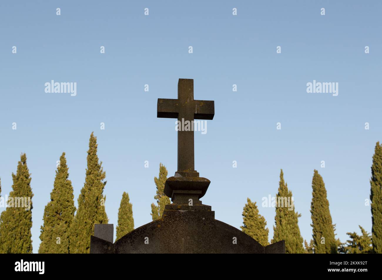 Catholic stone cross in the cemetery, with cypress trees in the ...