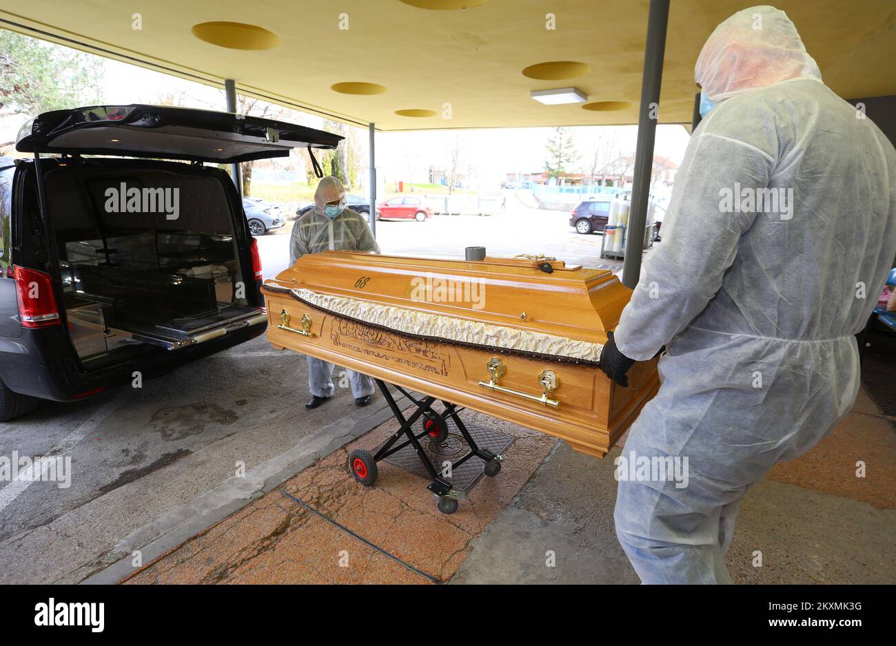 Funeral workers wearing protective suits move the coffin containing the ...