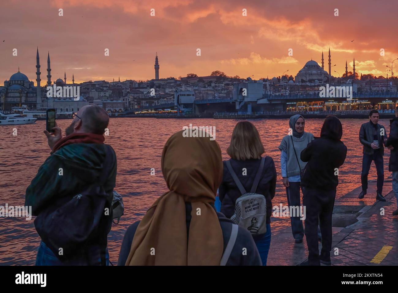 People take pictures of the setting sun behind the Suleymaniye Mosque ...