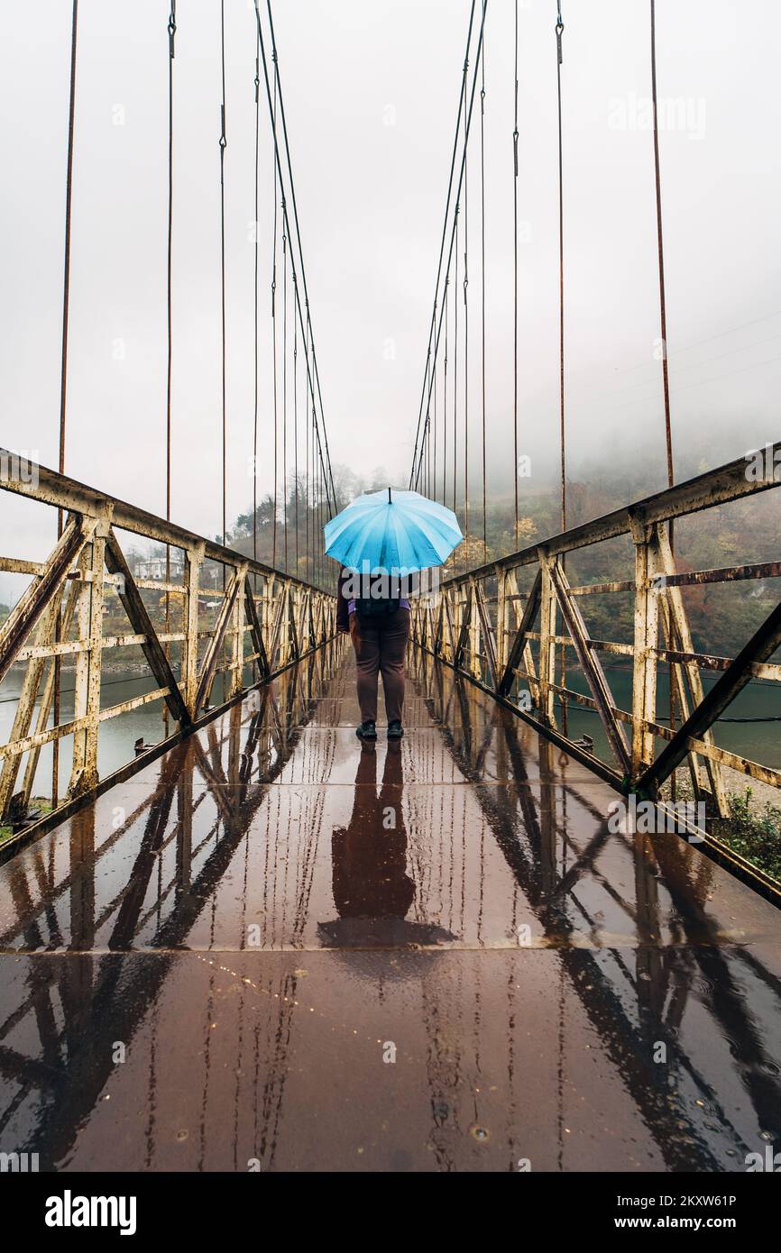 Girl with blue umbrella stands on wet iron suspension bridge in rainy ...