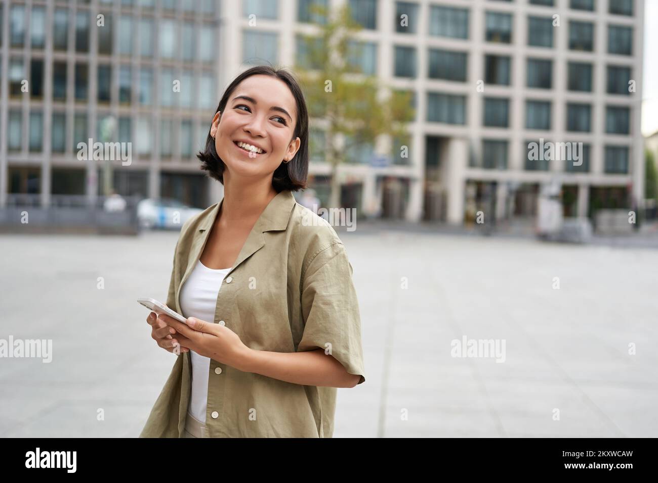 Portrait of asian woman standing on street, city square and holding ...
