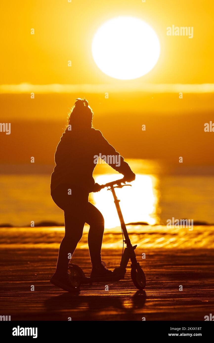A girl is silhouetted as she ride a scooter during a sunset in Split ...