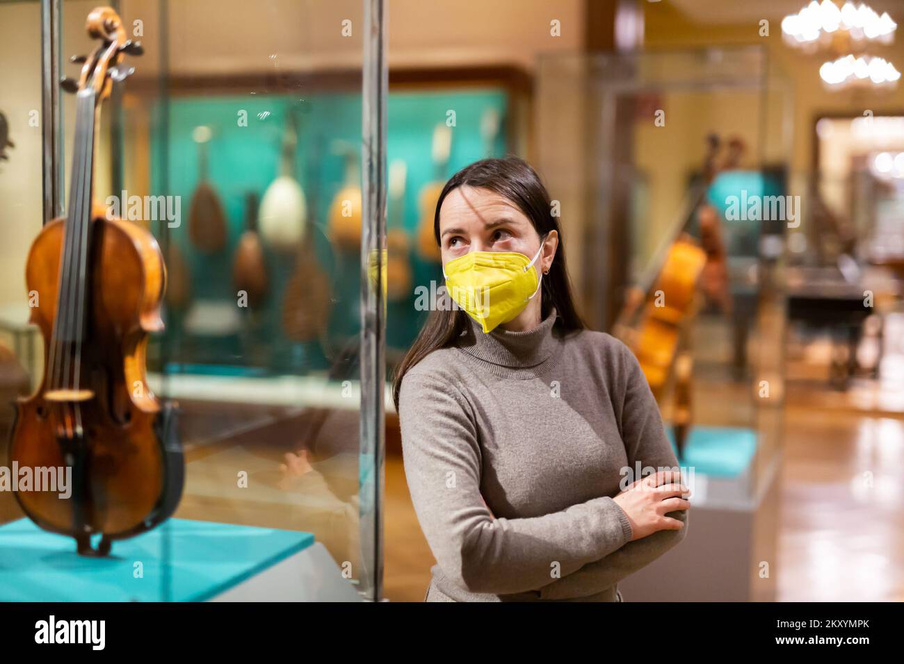 Female museum visitor in mask examining ancient musical instruments ...