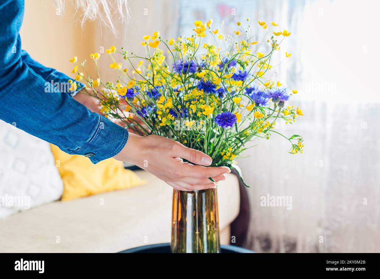 Close up of bouquet. Woman puts vase with blue and yellow flowers on ...