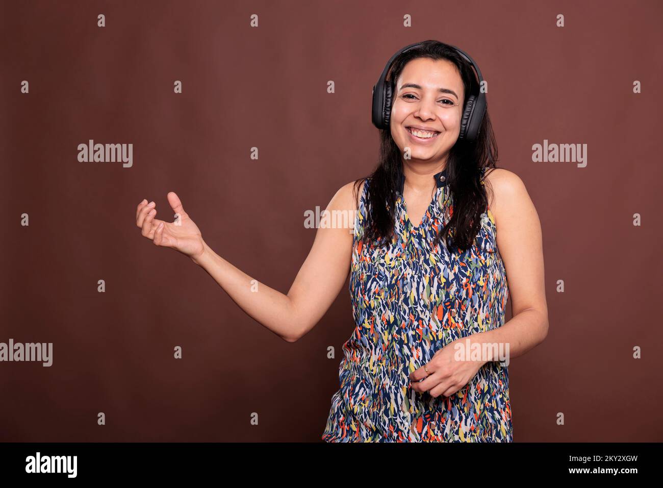 Smiling indian woman in headphones singing, looking at camera ...