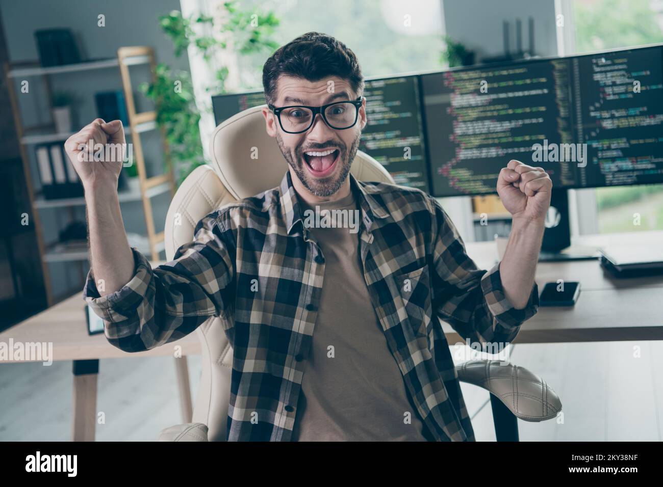 Portrait of delighted overjoyed person sit chair raise fists shout yes ...