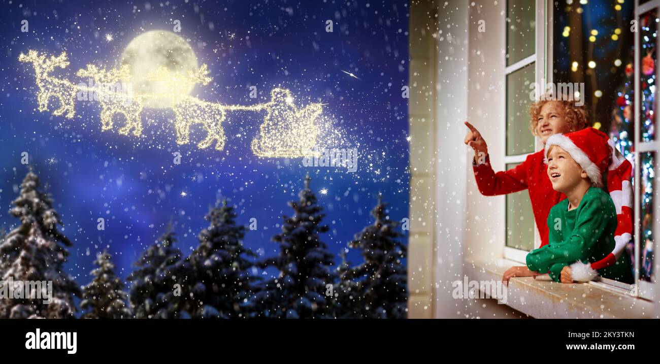 Kids look at Santa fly in the sky on Christmas eve. Children watch reindeer and Santa Claus ...