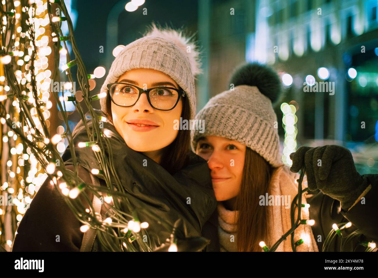 Two funny laughing young Girlfriends women with winter Christmas lights ...