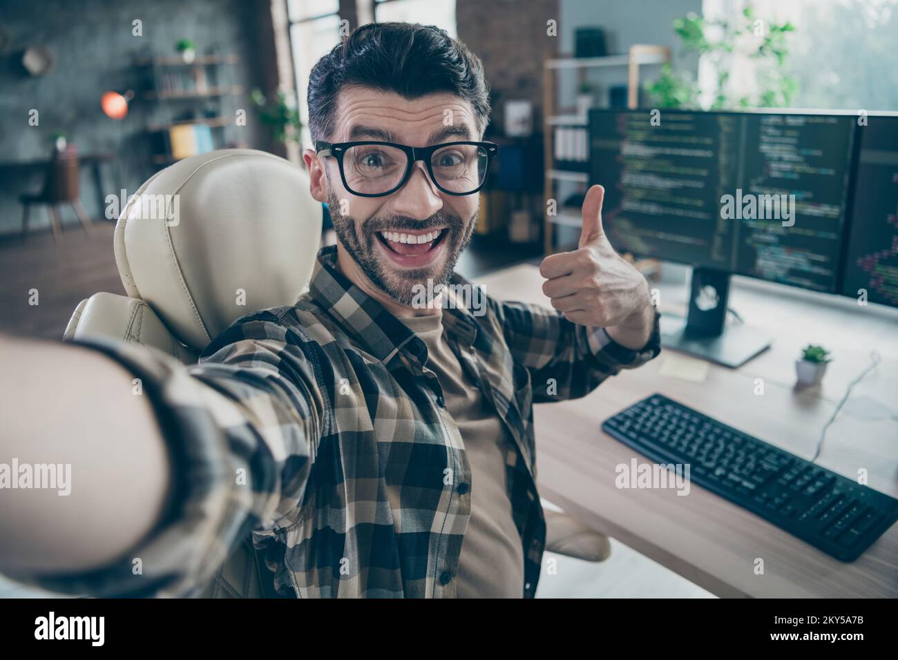 Portrait of excited crazy hacker man sit chair make selfie show thumb ...