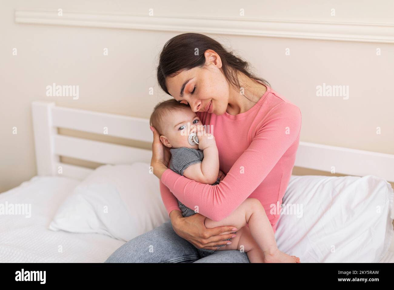 Portrait of loving mother resting with her infant baby girl in bed ...