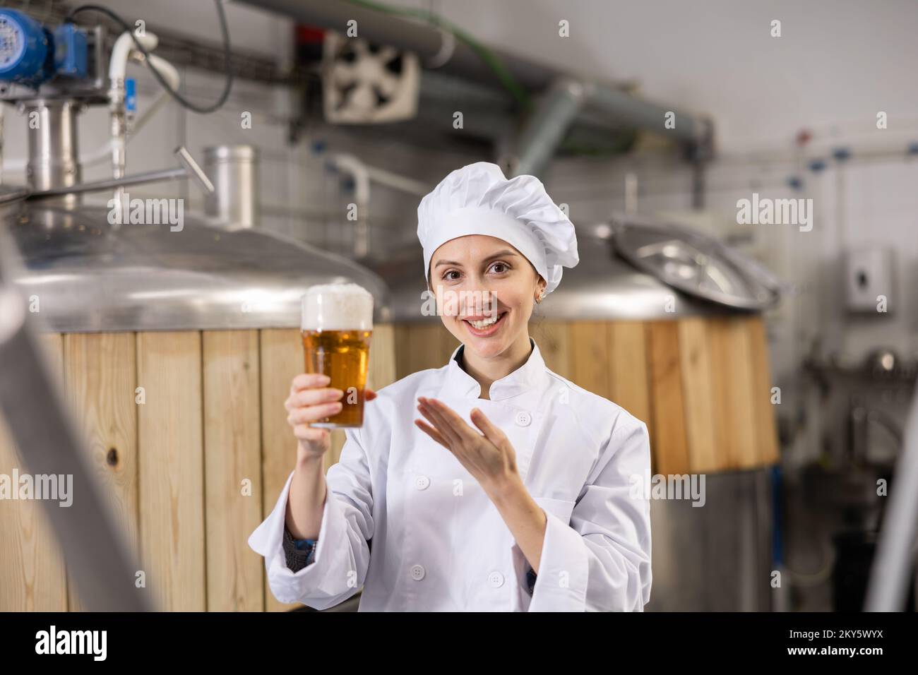 Female brewer is standing with beer with foam in glass on workplace ...