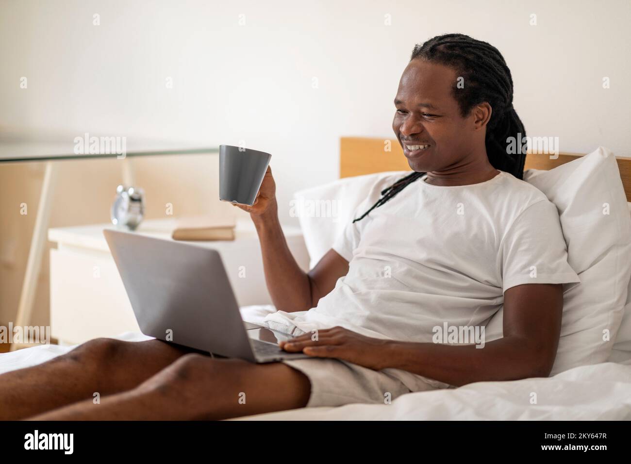 Smiling Young Black Man Resting In Bed With Laptop And Coffee Stock ...
