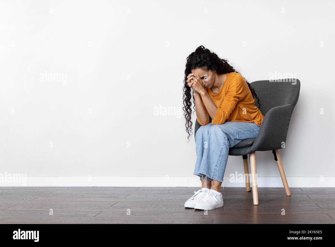 Upset curly brunette woman sitting in arm chair, crying Stock Photo - Alamy