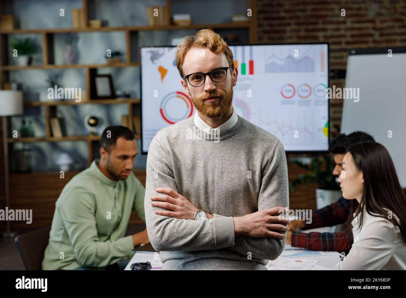 Confident smiling ginger guy, startup team leader, standing in front of ...