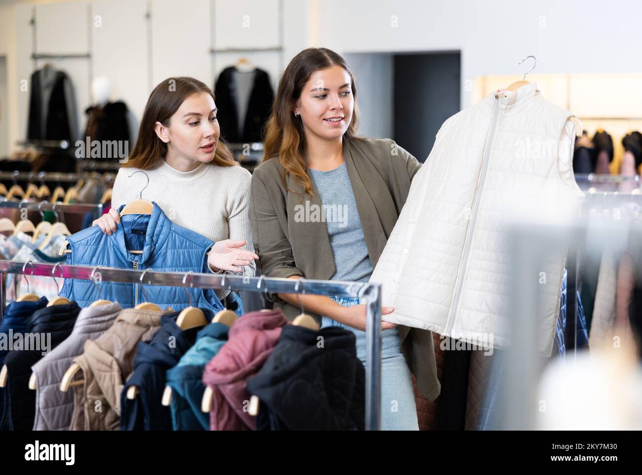 Joyful young women choosing between white and blue waistcoats in a ...