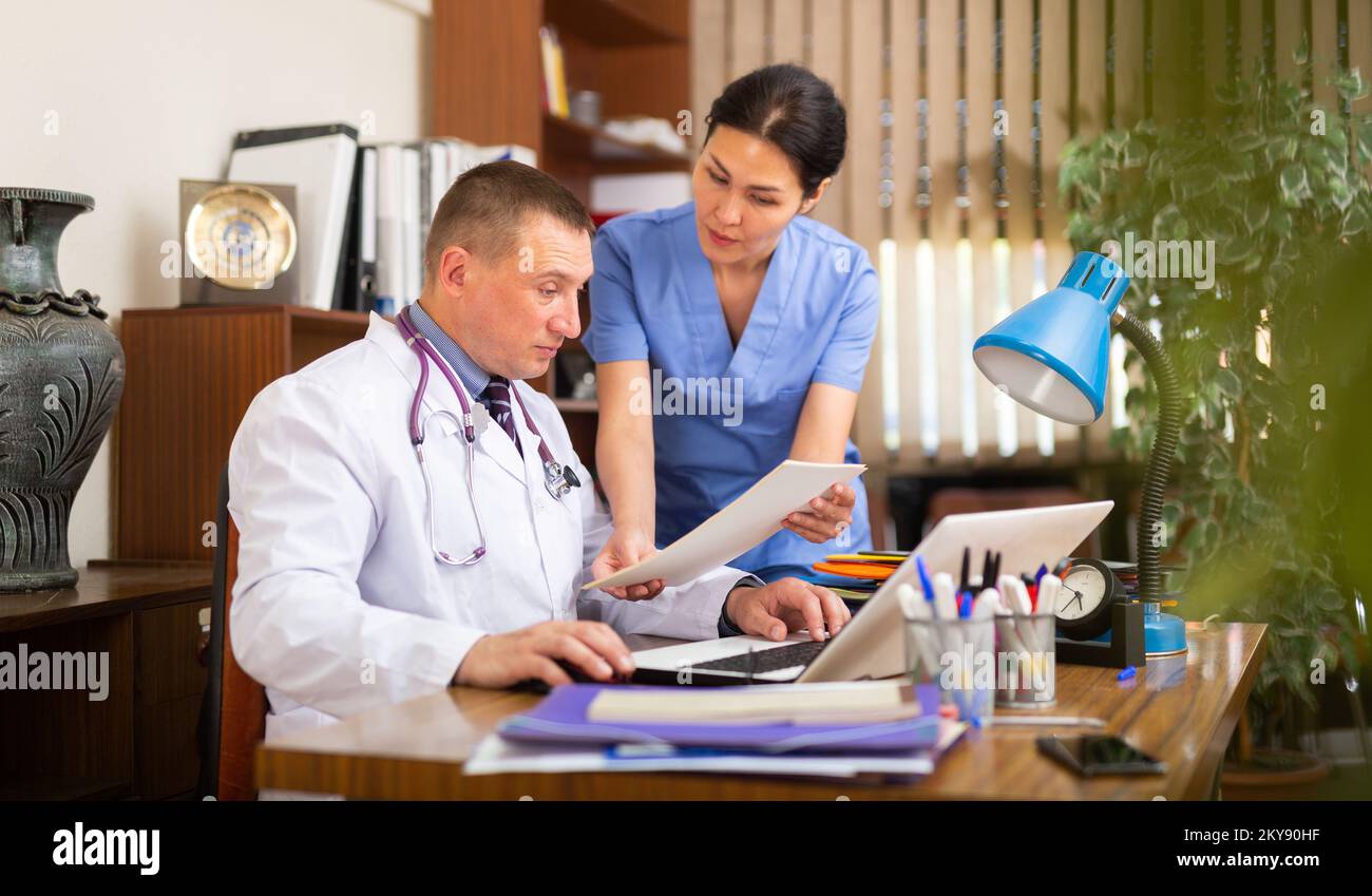 Two fellow doctors filling up medical forms on laptop in office Stock ...