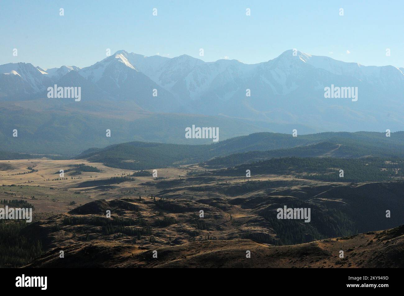 Hilly valley in the rays of the setting sun at the foot of snow-capped ...