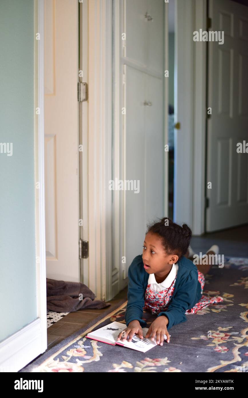 Young Girl Lying On Her Stomach In The Hallway While Reading A Book
