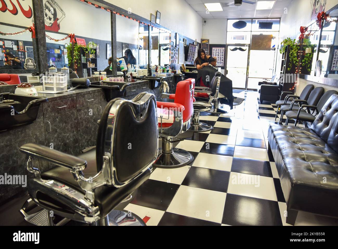 Wide view of a barber shop showing a Latina woman cutting a young black ...
