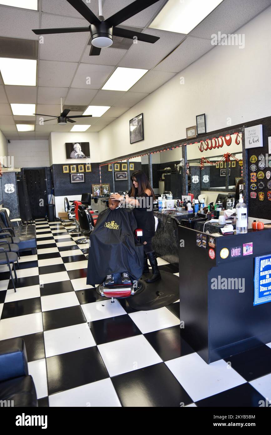 Photo of a barber with a Latina woman cutting a young black kid’s hair ...