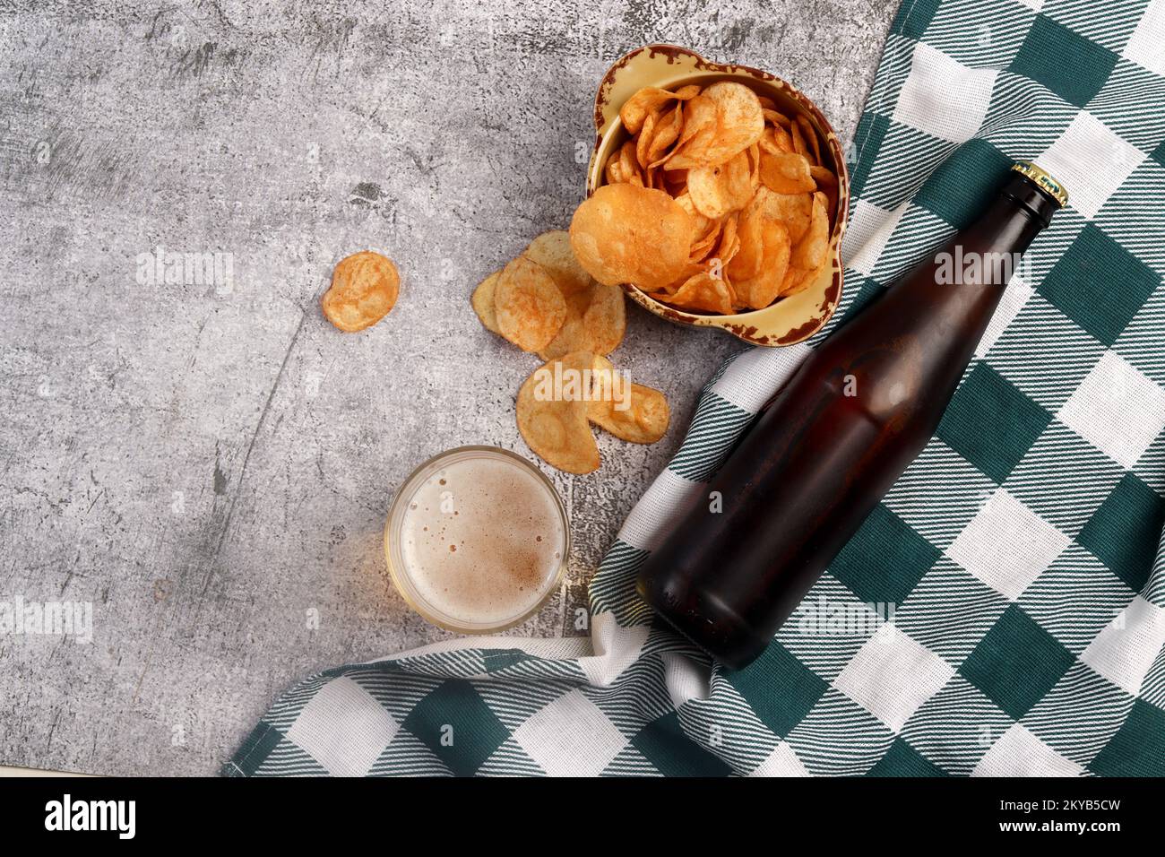 Сold beer in a bottle and glass and potato chips in a bowl on a dark ...