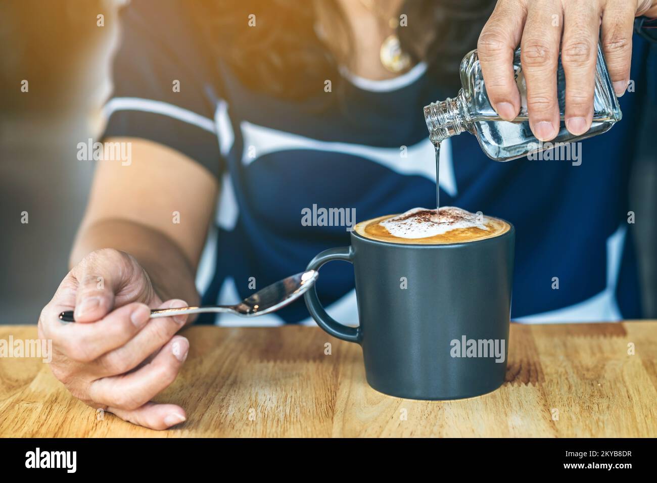Close up of mature woman pouring warm syrup into hot cappuccino on cafe ...
