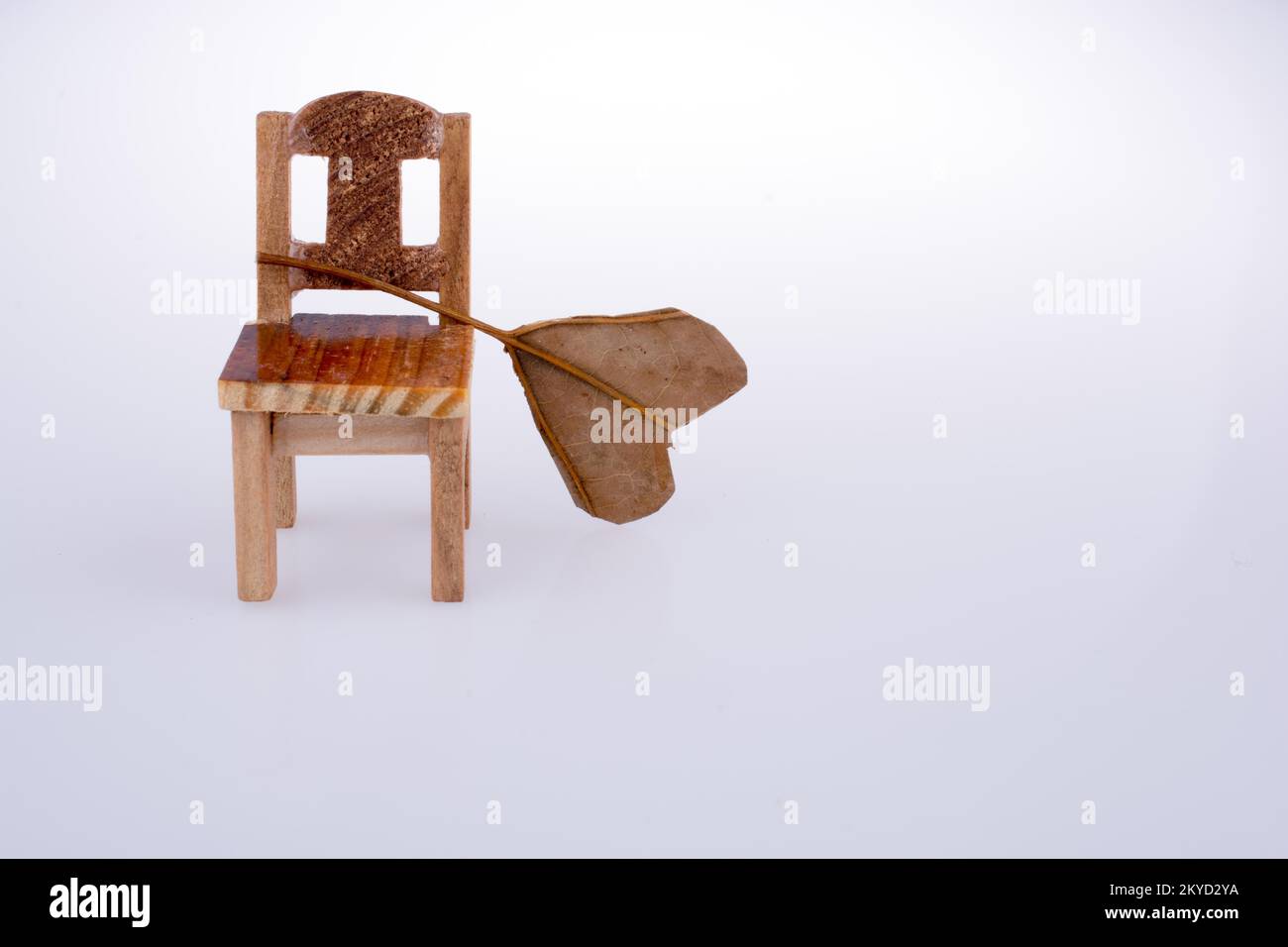 Heart shape cut dry leaf put on a little model chair on a white ...