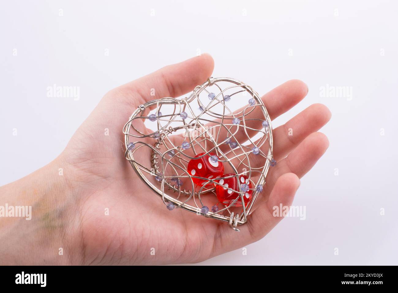 Hand holding Red dice in a heart shaped cage on a white background ...