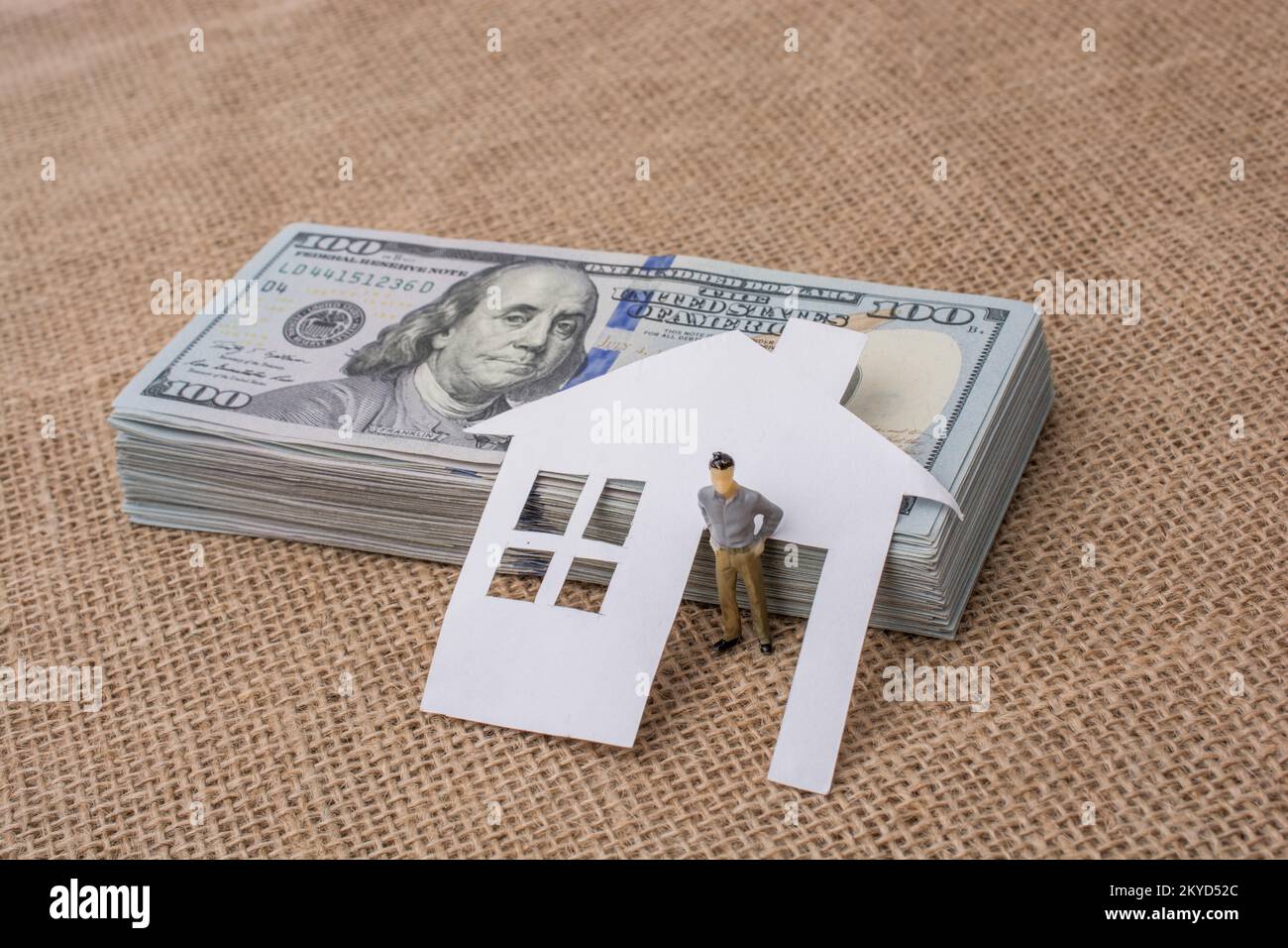 Paper house and a man figurine beside a bundle of US dollar banknote ...