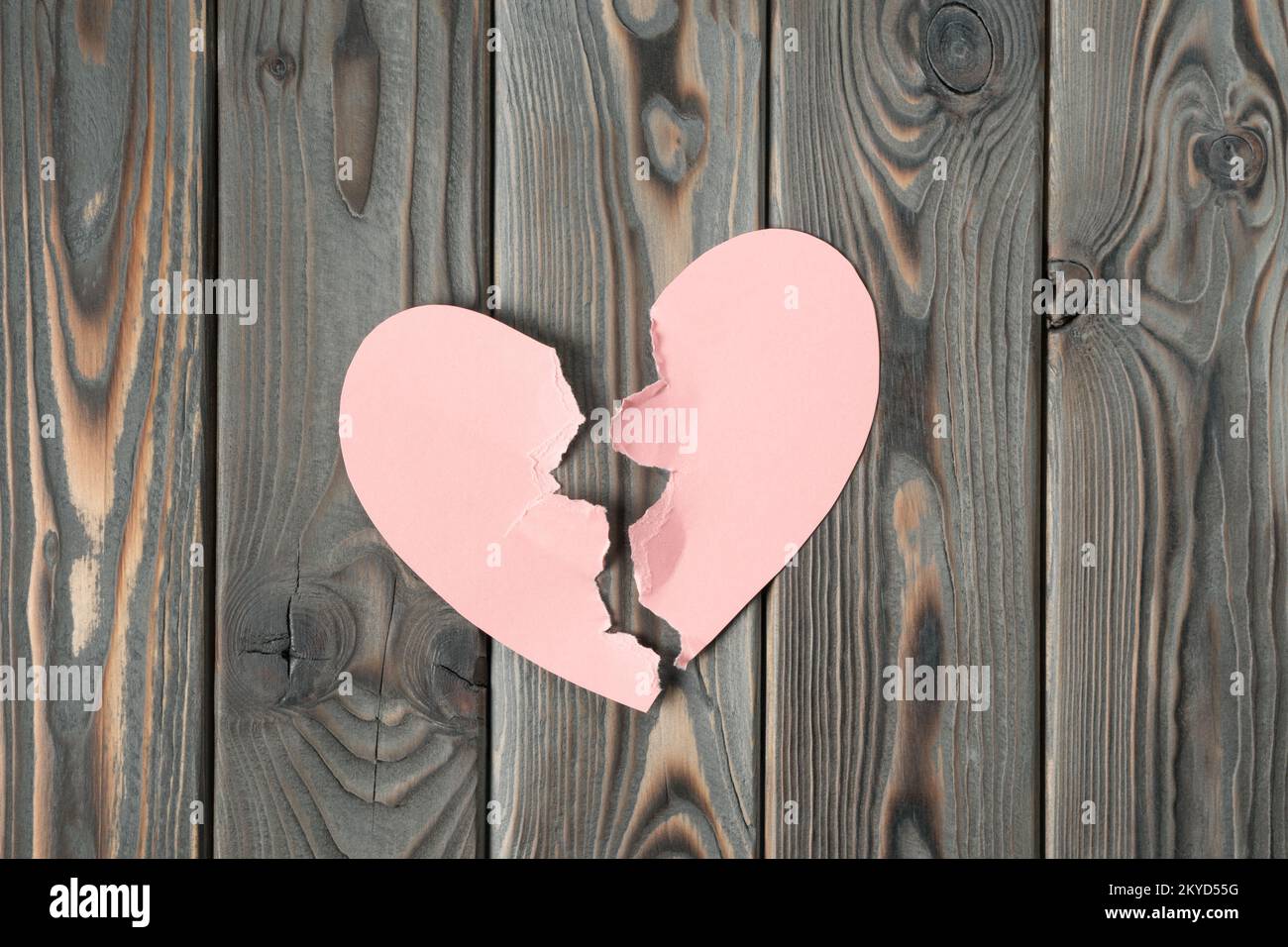 Pink torn paper heart halves laying together on dark wooden table ...