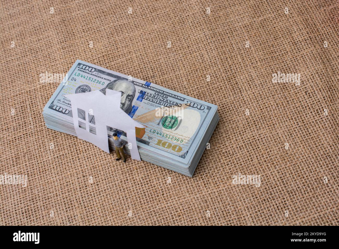 Paper house and a man figurine beside a bundle of US dollar banknote ...