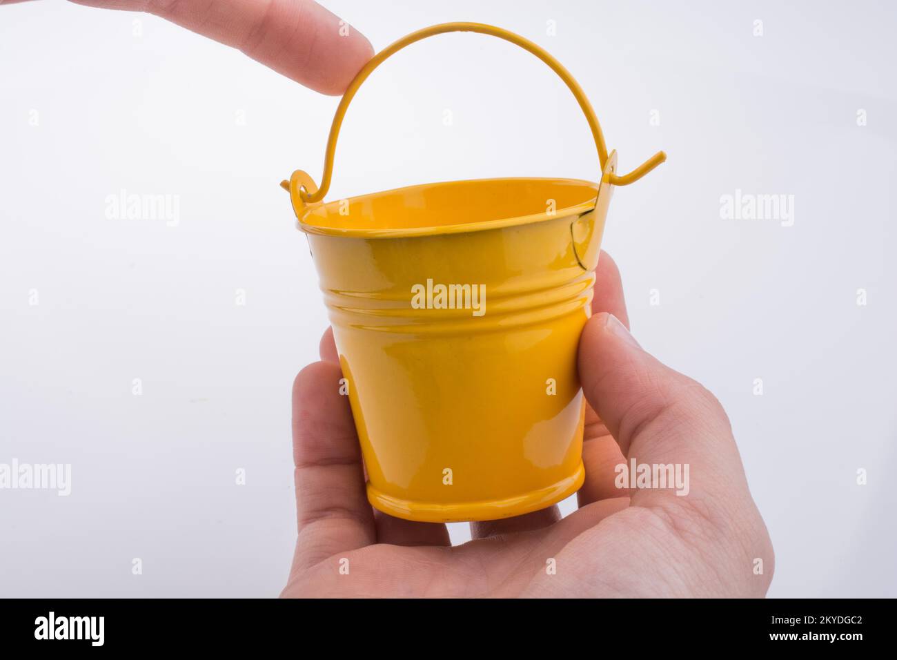 Hand holding a yellow bucket on a white background Stock Photo - Alamy