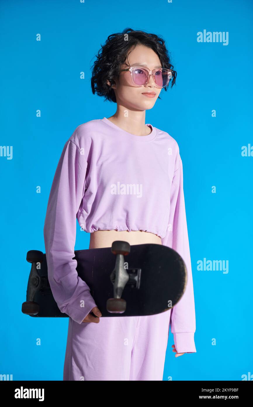 Portrait of teenage girl with skateboard standing against blue ...