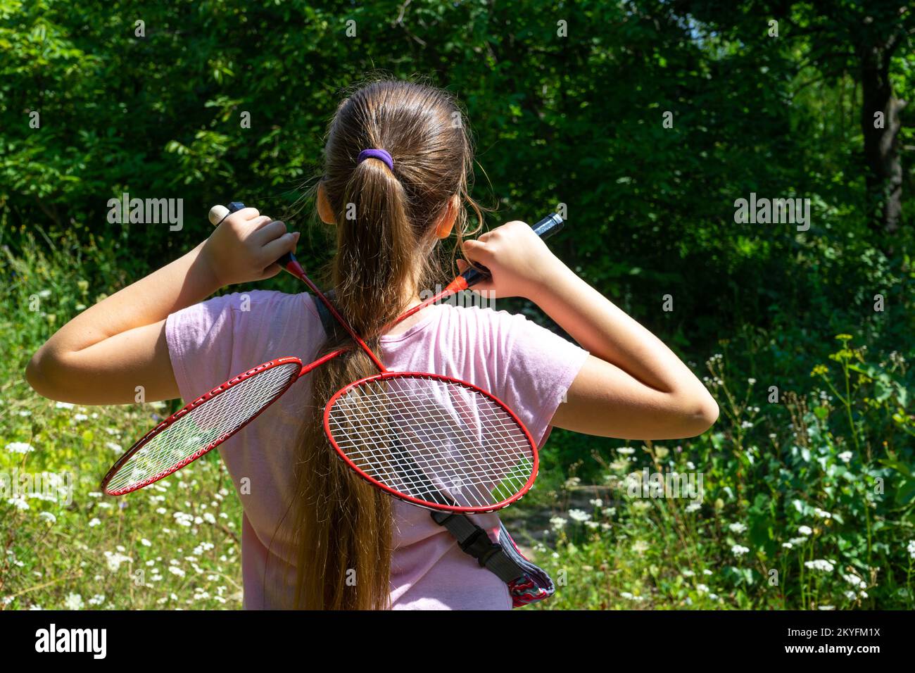 A girl stands in a forest clearing with two tennis rackets crossed on ...