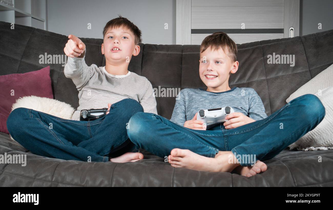 Happy teenagers sit on sofa with game joysticks. Children play ...
