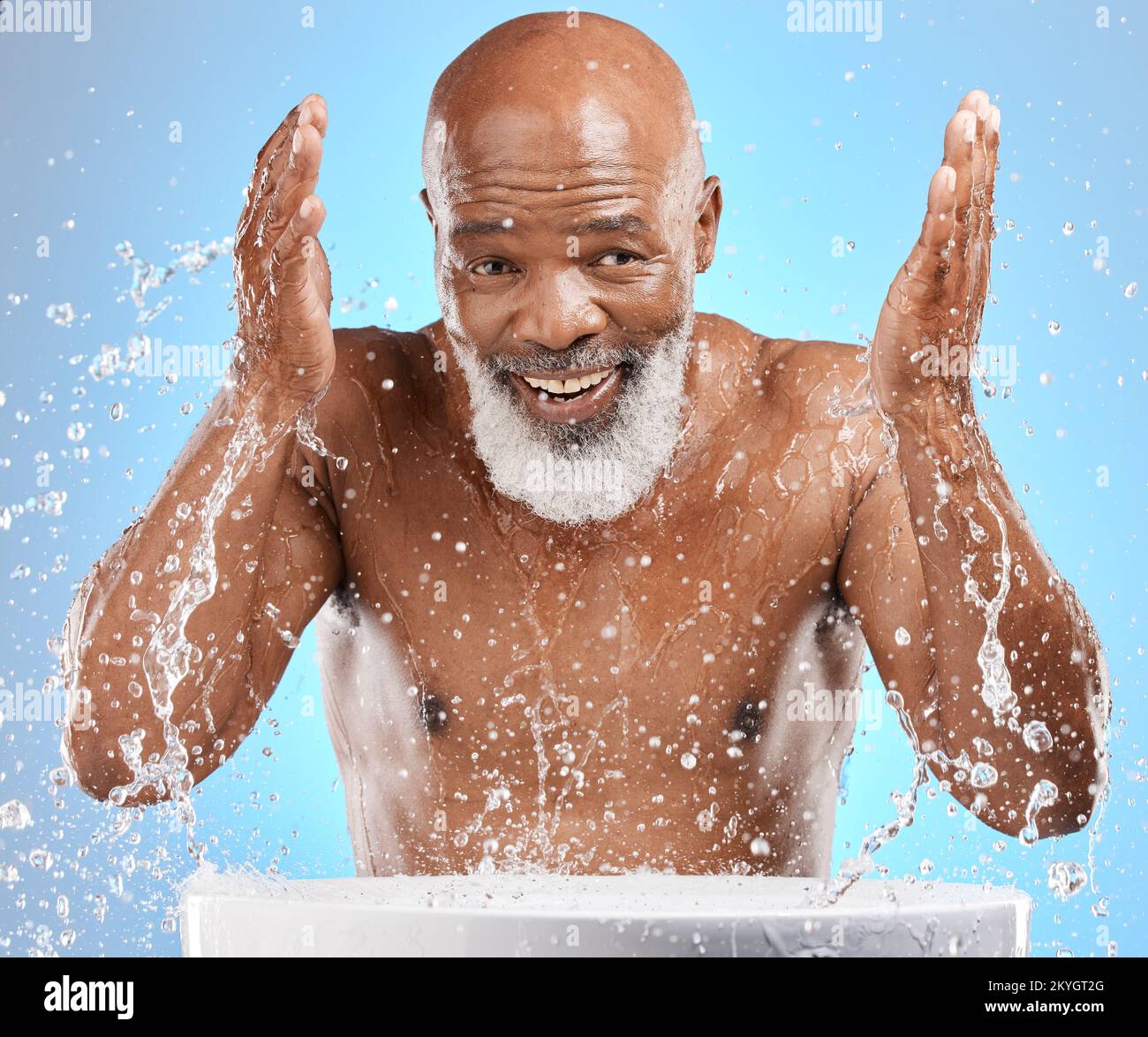 Water splash, senior and black man cleaning face in studio isolated on a blue background ...