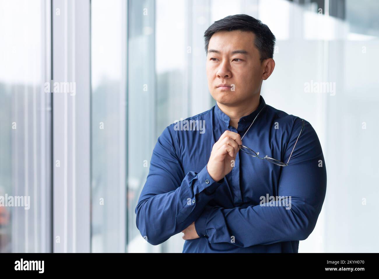Thinking Asian businessman, man in shirt and glasses near office window ...