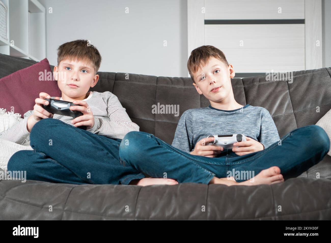 Cute school aged boys sit on sofa with game joysticks. Children play ...