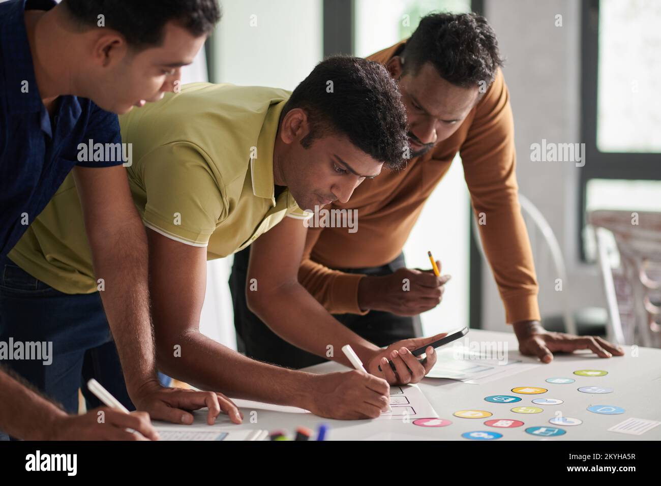 Team of UX designers leaning over big table when creating new interface ...